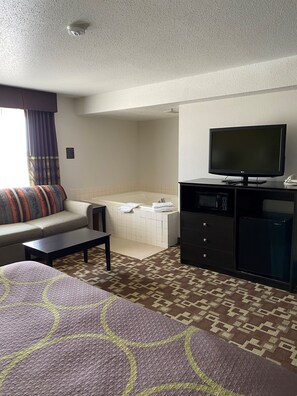 Quarto de hotel com sofá, televisão, mesa pequena, armário e banheira.