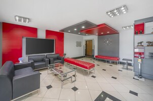 Um hall moderno com uma televisão de tela plana grande, sofás de couro, uma mesa de centro de vidro, bancos vermelhos e um balcão de recepção.