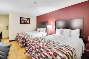 Quarto de hotel com duas camas, uma escrivaninha, uma cadeira, um abajur e um quadro na parede.