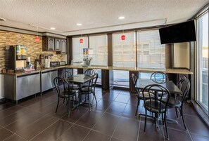 Um restaurante com balcão de cozinha, mesas para refeições, cadeiras e uma televisão na parede.