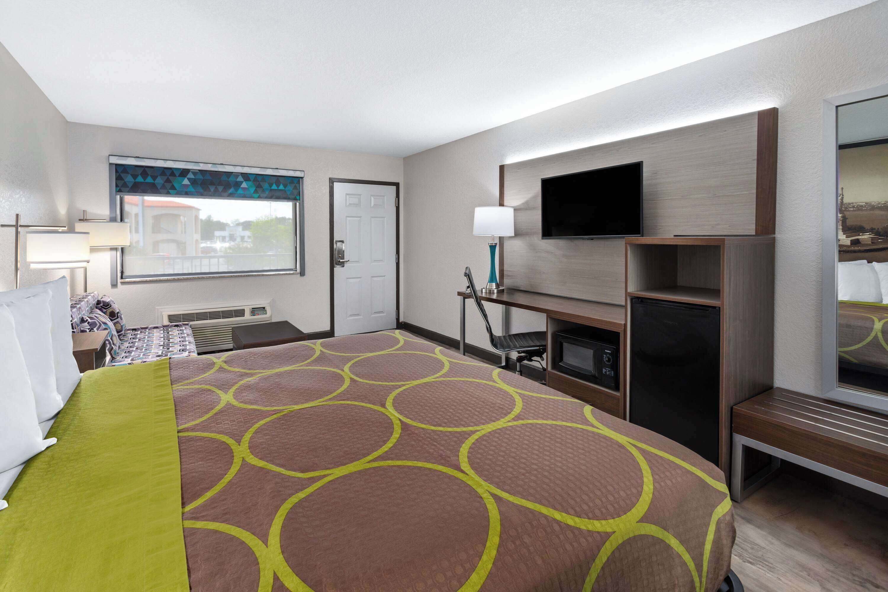 Quarto de hotel com cama, televisão, escrivaninha e janela com vista.