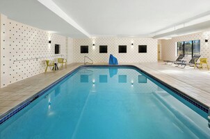Piscina interna com chão revestido em azulejo, água azul e cadeiras amarelas.