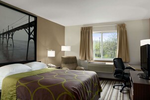 Quarto de hotel com cama, escrivaninha com cadeira, televisão e janela com cortinas.