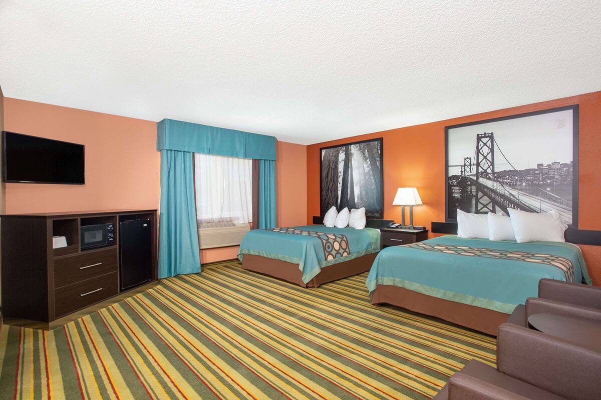 Quarto de hotel com duas camas, televisão, secretária e janela com cortinas.