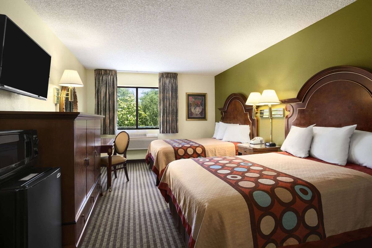 Quarto de hotel com duas camas, uma escrivaninha, uma televisão e uma janela com cortinas.