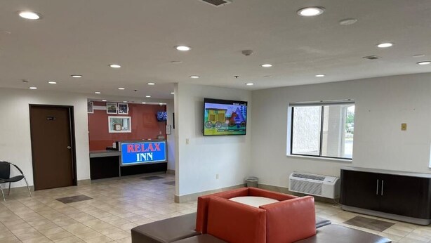 Um saguão de hotel com um sofá de couro marrom, uma TV fixada na parede e uma placa para o Relax Inn.