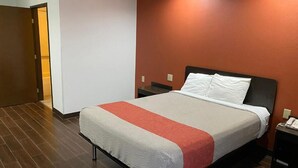 Quarto de hotel com uma cama, uma mesa de cabeceira e uma porta para outro cômodo.