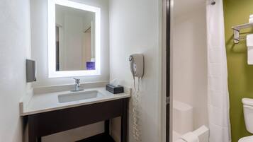 Casa de banho com lavatório branco, espelho, secador de cabelo e cortina de chuveiro.