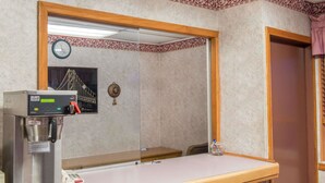 Quarto de hotel com um espelho grande, uma máquina de café, um relógio e uma porta com cortina.