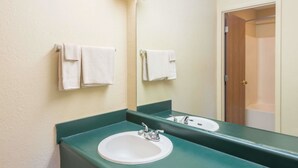 Casa de banho com uma pia branca, bancada verde e um espelho a refletir uma porta e uma banheira.