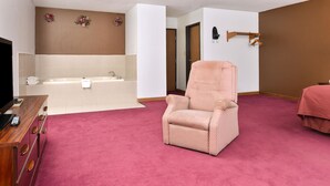 Quarto com uma banheira grande, penteadeira de madeira, poltrona rosa e cama com colcha vermelha.