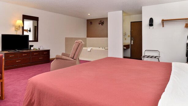 Quarto de hotel com uma cama grande, uma cadeira, uma escrivaninha com televisão, um banheiro com banheira e um porta-roupas.