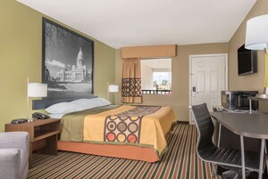 Quarto de hotel com cama, escrivaninha, cadeira, televisão e uma janela grande.