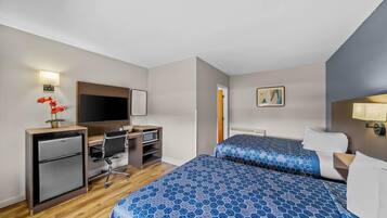 Quarto de hotel com cama, escrivaninha com computador, frigorífico, televisão e candeeiro de parede.