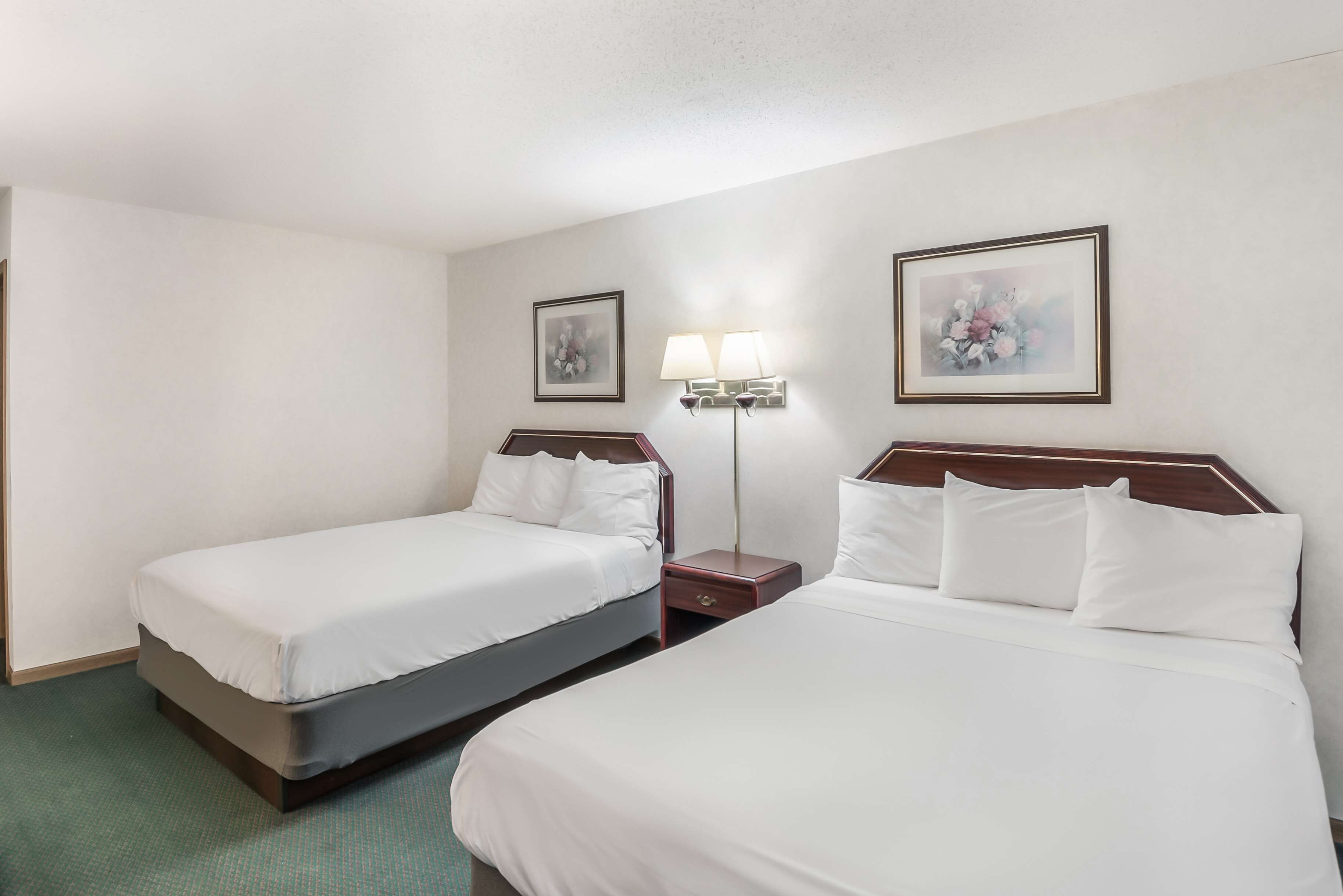 Quarto de hotel com duas camas de solteiro, mesa de cabeceira com abajur e quadros nas paredes.
