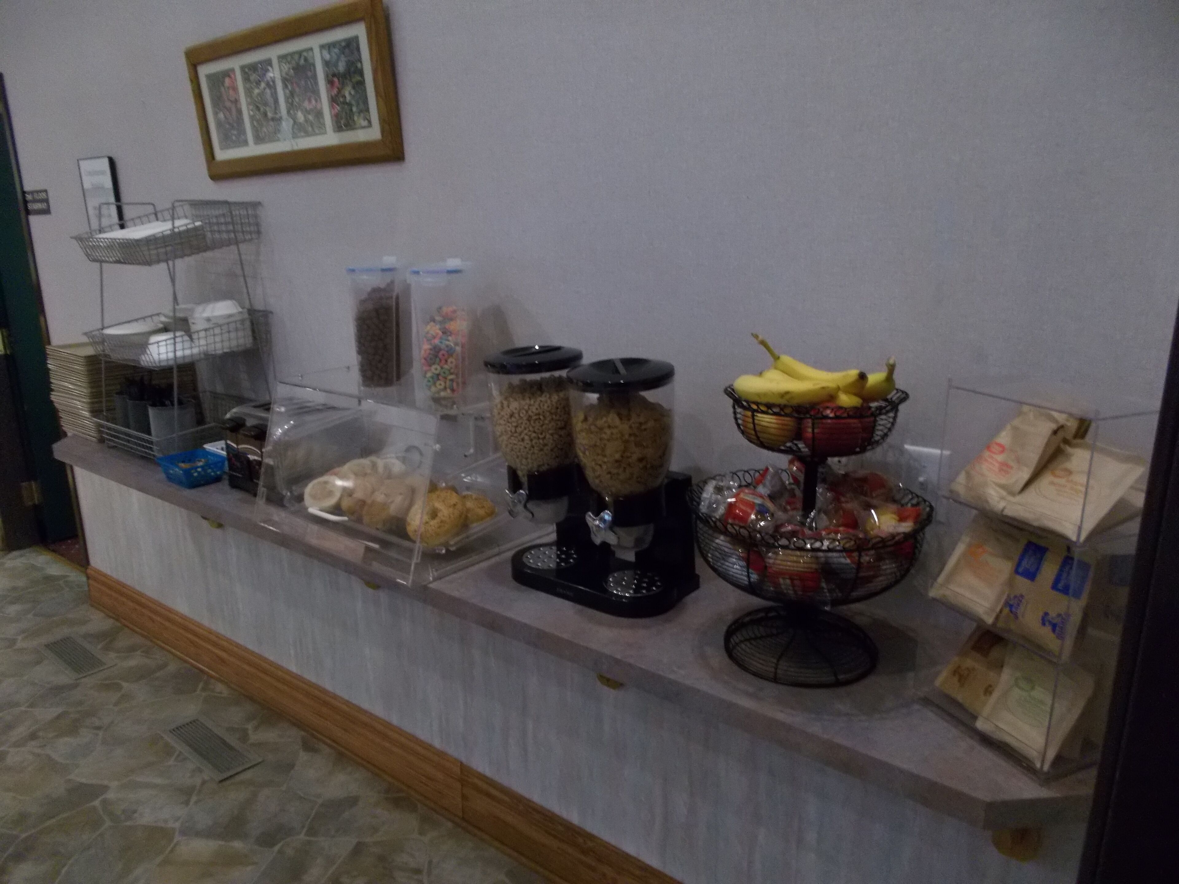 Balcão de buffet com diversos alimentos e recipientes, incluindo cereais, biscoitos e uma cesta de frutas.