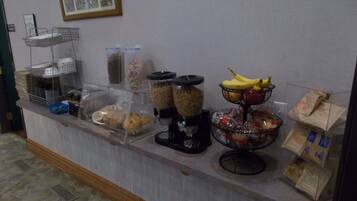 Balcão de buffet com diversos alimentos e recipientes, incluindo cereais, biscoitos e uma cesta de frutas.