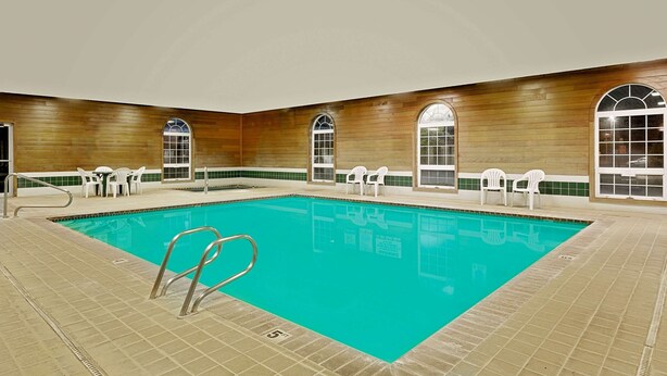 Piscina interior com água cristalina, rodeada por paredes de madeira e janelas em arco.