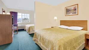 Quarto de hotel com cama grande, escrivaninha, cadeira, janela com cortinas e um quadro na parede.