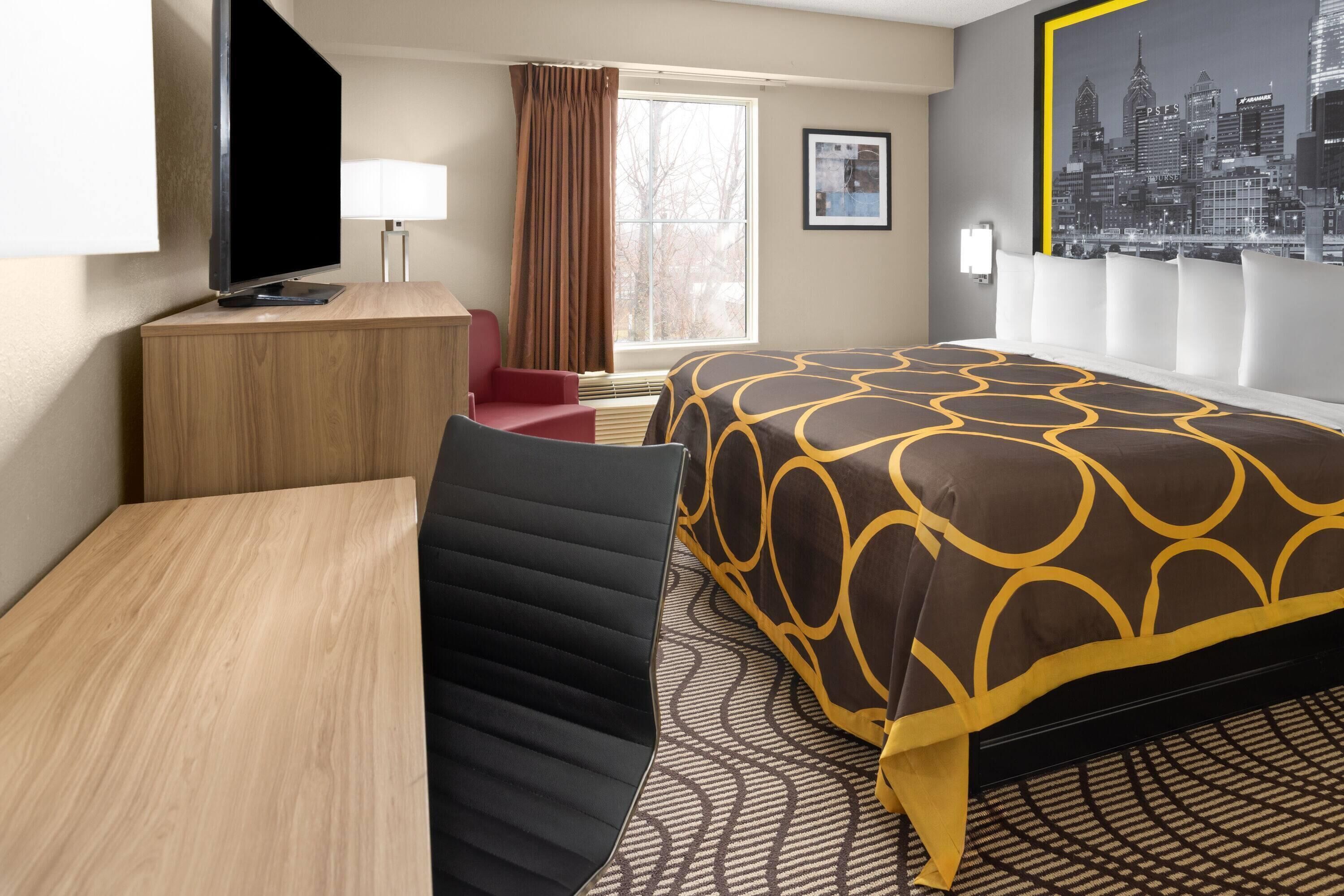 Quarto de hotel com cama, escrivaninha, televisão, janela com cortinas e vista para a cidade.