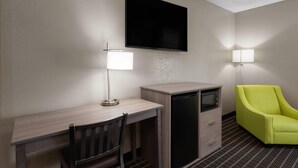 Quarto de hotel com escrivaninha, cadeira, televisão, micro-ondas e uma cadeira verde vibrante.
