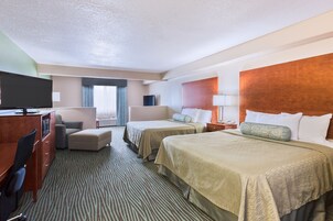 Quarto de hotel com duas camas, uma mesa de trabalho, uma televisão, uma cadeira e uma janela com cortinas.