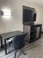 Quarto de hotel moderno com televisão de tela plana na parede, escrivaninha de madeira escura e cadeira de escritório preta.