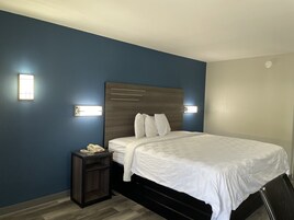 Quarto de hotel com uma cama grande, mesa de cabeceira com telefone e luminárias fixadas na parede.