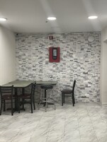 Uma sala de jantar com piso de mármore, uma mesa com quatro cadeiras e um letreiro de saída de emergência vermelho na parede.