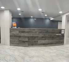 Uma receção com um painel de madeira cinzenta, pilares brancos e chão de mármore.