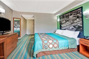 Quarto de hotel com uma cama, televisão, cômoda e um quadro de barcos na parede.