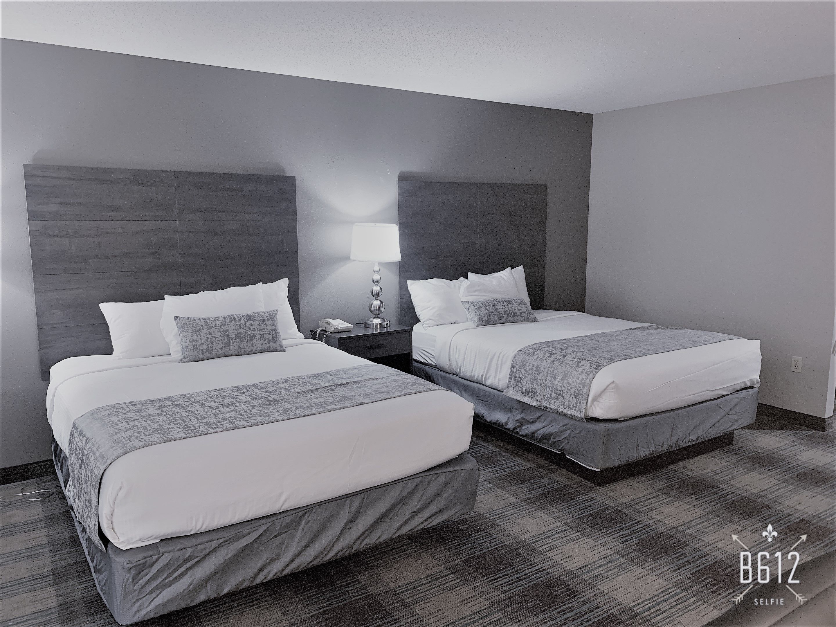 Quarto de hotel com duas camas, cabeceiras cinzentas, roupa de cama branca e um tapete cinza.