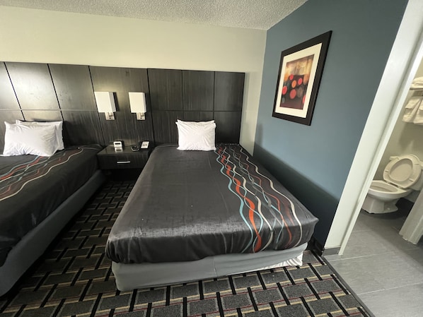 Quarto de hotel com duas camas, cabeceiras, mesas de cabeceira, telefone e um quadro na parede.
