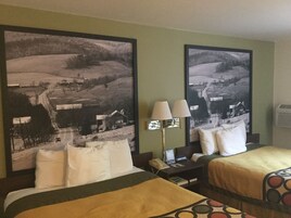 Quarto de hotel com duas camas, uma mesa de cabeceira com abajur, telefone e uma pintura em preto e branco de paisagem emoldurada na parede.