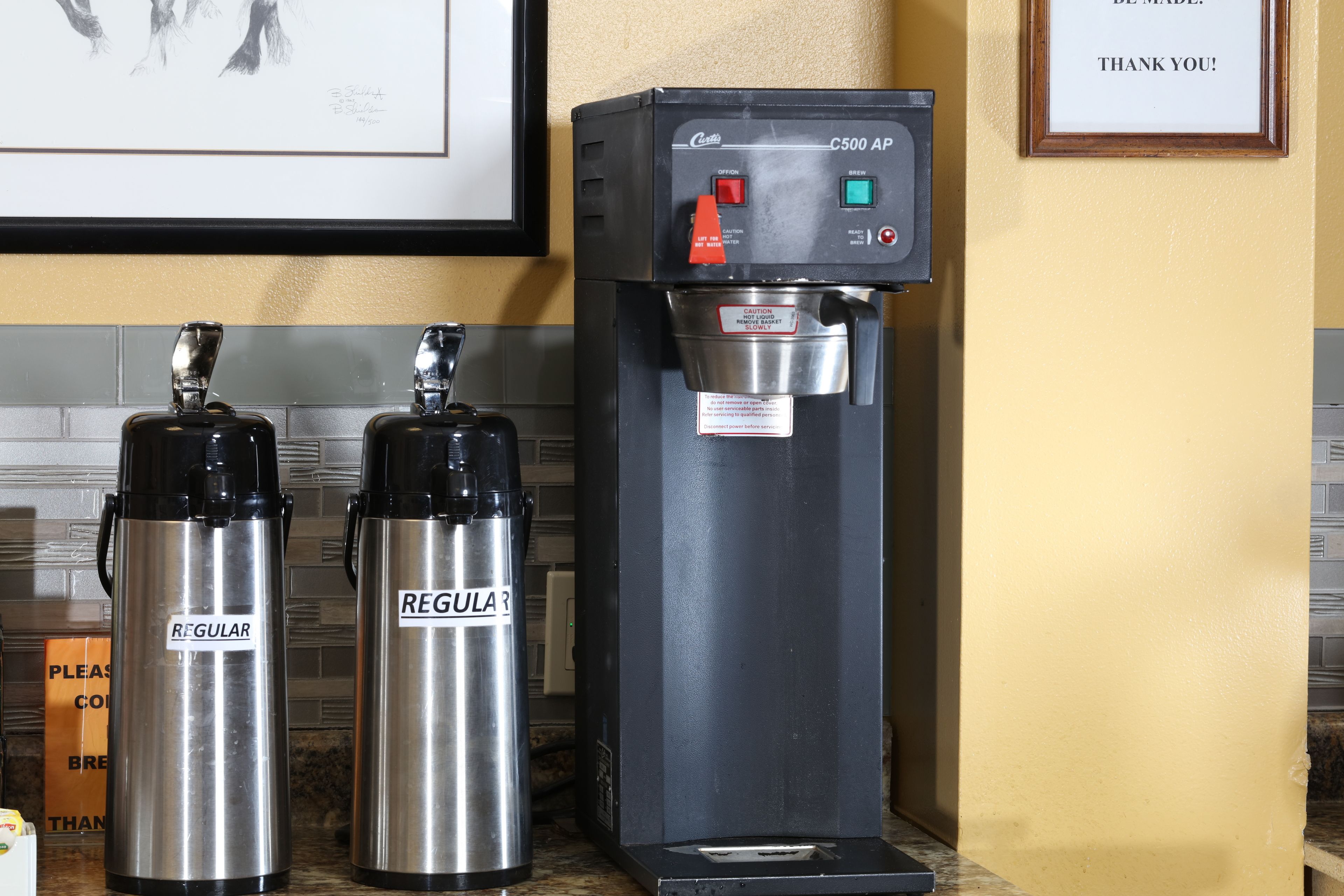 Máquina de café e duas garrafas térmicas isoladas com a etiqueta 'Regular' sobre uma bancada.