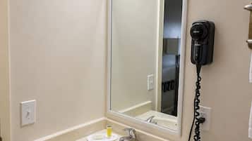 Casa de banho com lavatório, espelho e secador de cabelo fixado na parede.