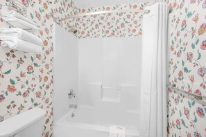 Um chuveiro com papel de parede estampado com flores, uma banheira branca e um vaso sanitário.