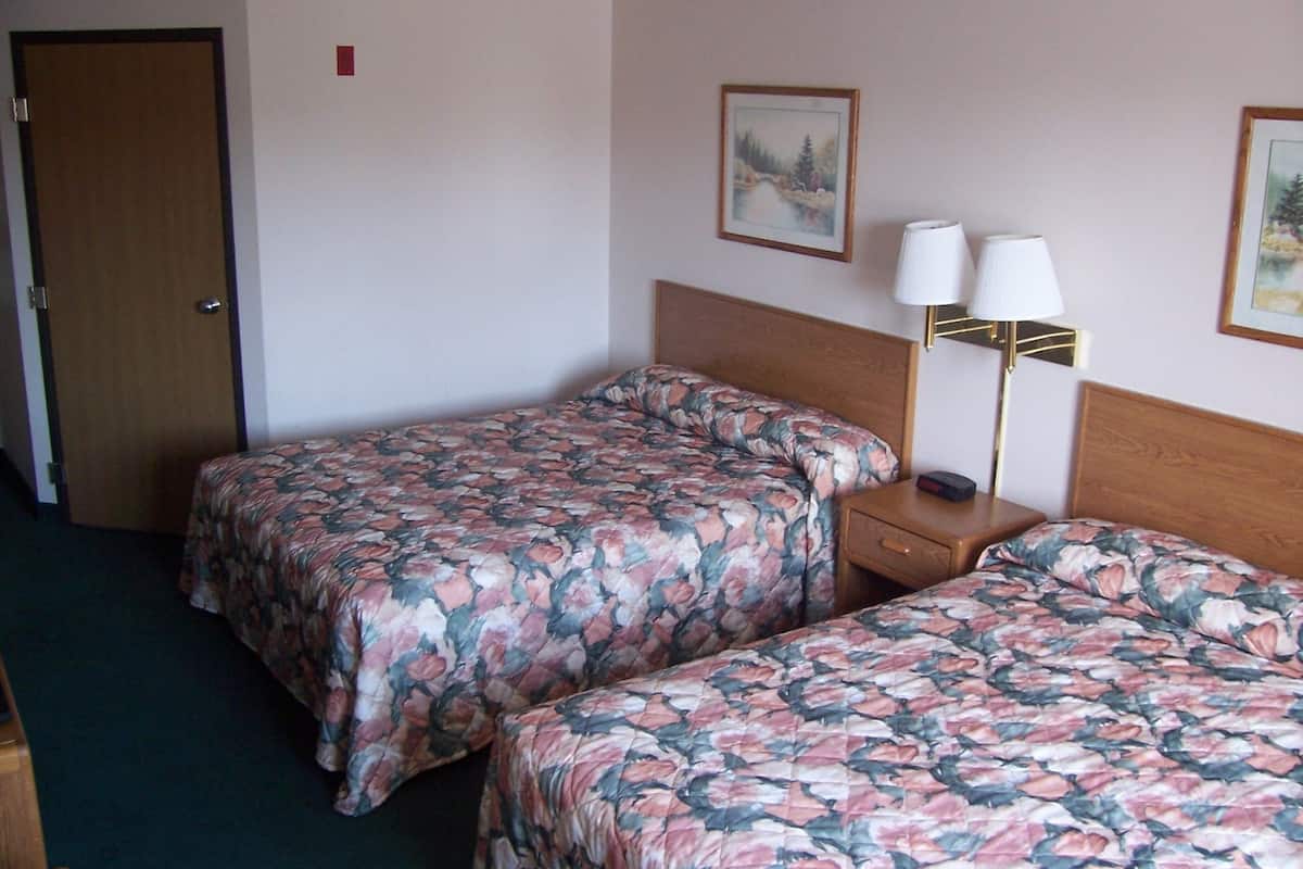 Quarto de hotel com duas camas, uma mesa de cabeceira, uma luminária e uma porta.