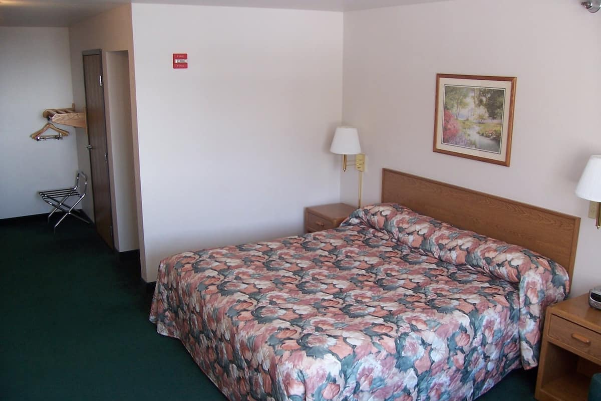 Quarto de hotel com uma cama, duas mesas de cabeceira, um criado-mudo, uma luminária, um quadro na parede e um sinal de saída de incêndio.
