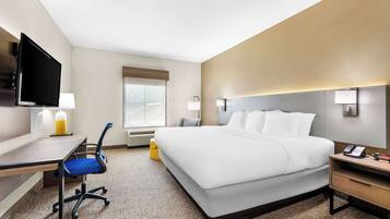 Quarto de hotel com cama, escrivaninha, cadeira, televisão, abajures e janela.