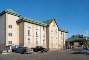 Um hotel de vários andares com telhado verde e um letreiro chamativo 'Holiday Inn Express'. Vários veículos estão estacionados na frente, incluindo uma caminhonete e um sedã.
