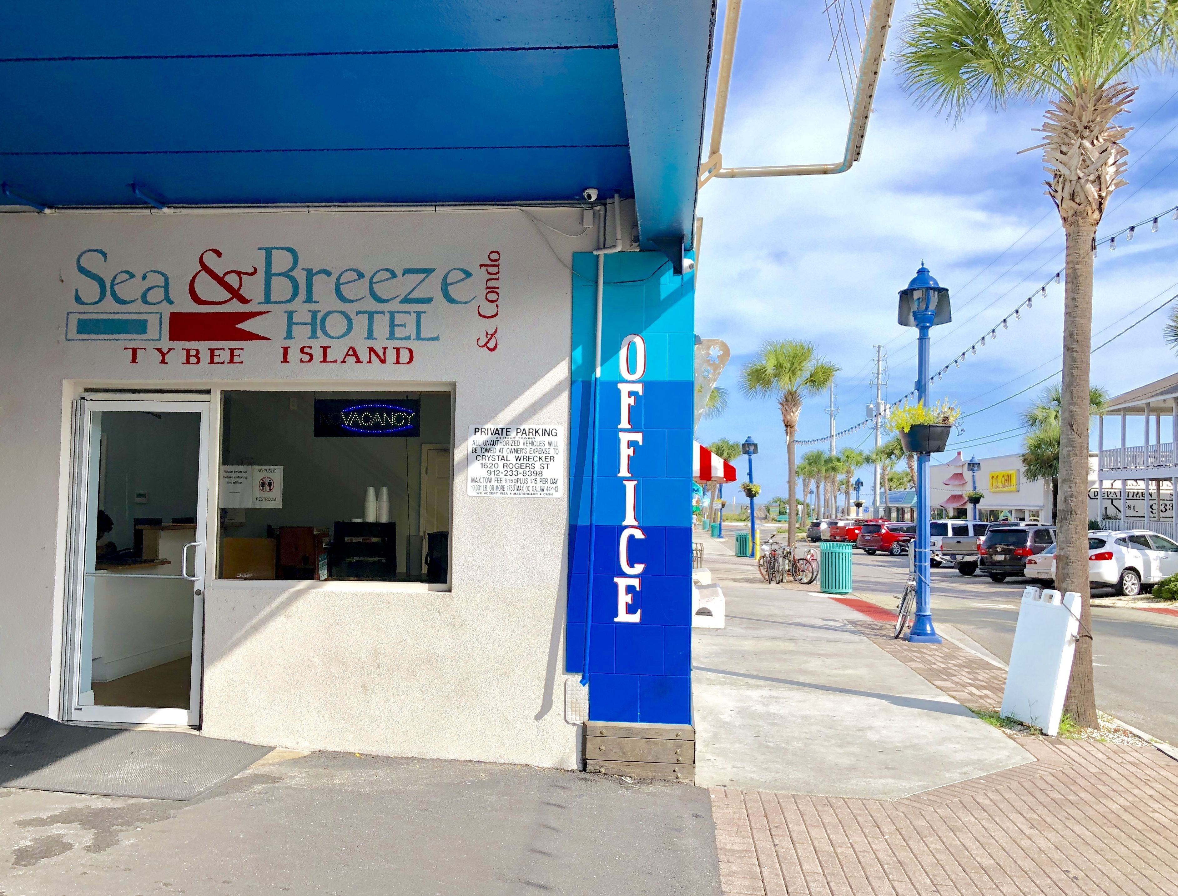 Exterior do Hotel Sea & Breeze Tybee Island, com um aviso de 'VACANCY' visível e um posto de estacionamento particular.