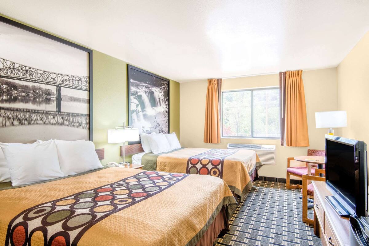 Quarto de hotel com duas camas, televisão, escrivaninha com cadeira e janela com cortinas.