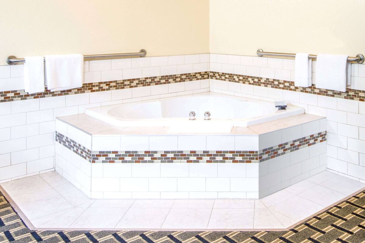 Um banheiro moderno com banheira independente, paredes com azulejos brancos e borda de mosaico.