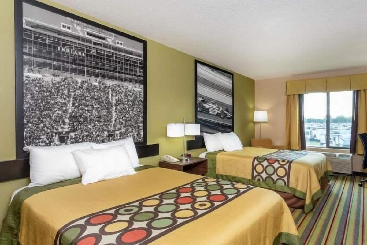 Quarto de hotel com duas camas, uma escrivaninha, uma cadeira, janela com vista e uma fotografia grande em preto e branco na parede.