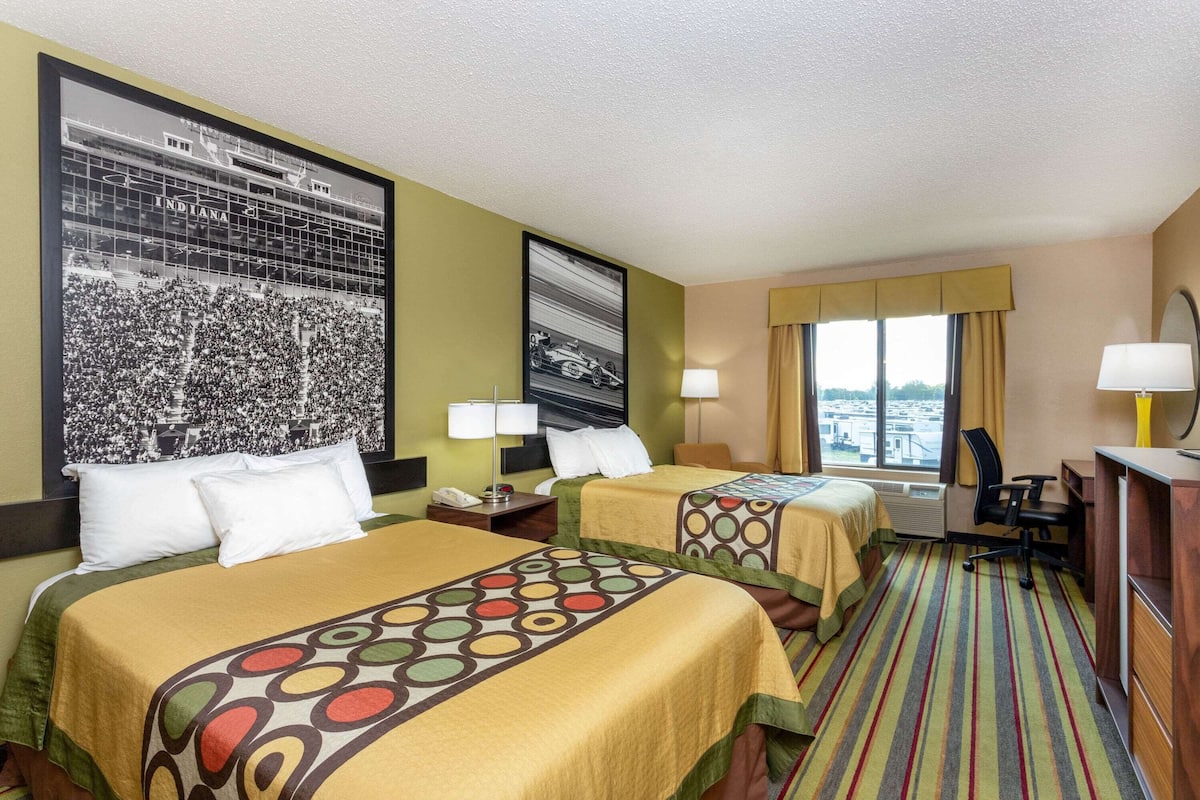 Quarto de hotel com duas camas, uma escrivaninha, uma cadeira e janela com vista.