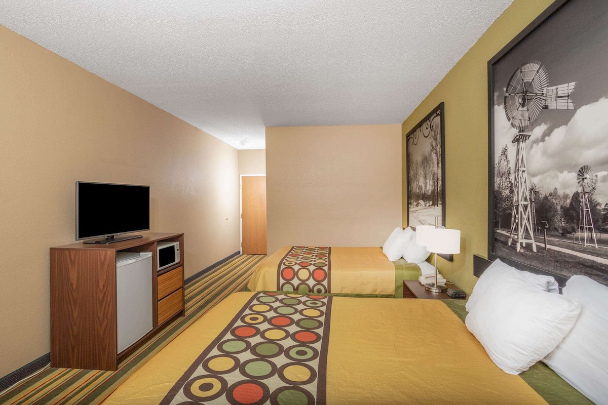 Quarto de hotel com duas camas, televisão, um pequeno frigorífico e um quadro de moinho de vento na parede.
