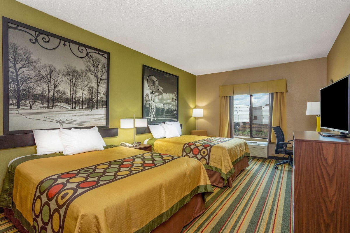 Quarto de hotel com duas camas, televisão, escrivaninha e janela com cortinas.