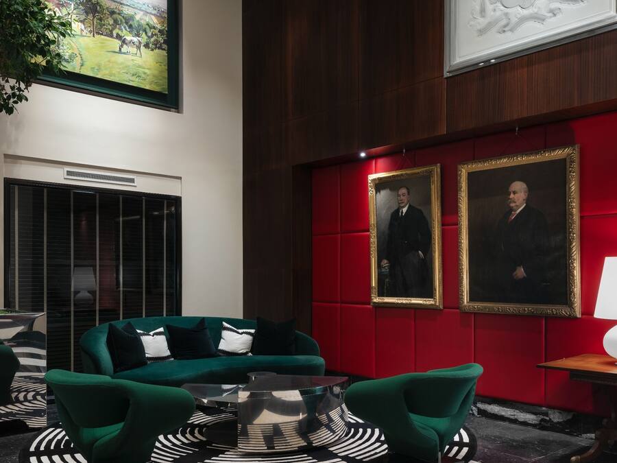 Um lobby moderno com sofás verdes, uma parede acolchoada vermelha e dois retratos emoldurados.