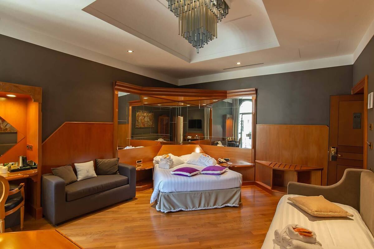 Quarto de hotel moderno com uma cama grande, um sofá, uma escrivaninha e um espaço de refeições.